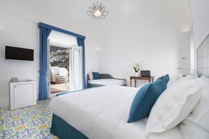 Quarto de hotel com cama, escrivaninha, poltrona, TV e vista para a paisagem urbana.