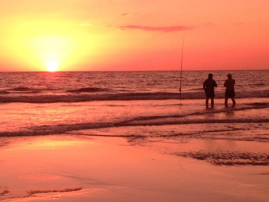 Pôr do sol sobre o oceano com duas pessoas pescando.