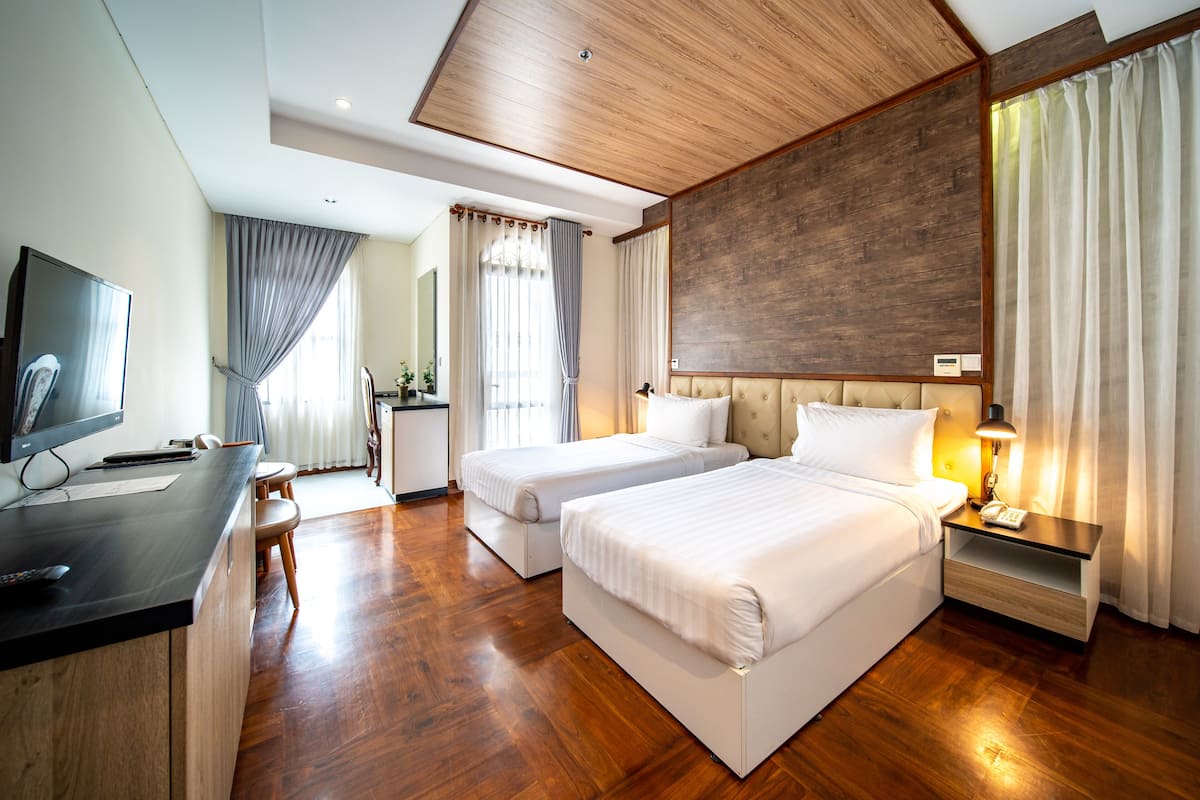 Quarto de hotel com duas camas, uma mesa de escritório com computador, televisão e mesa de cabeceira com abajur.