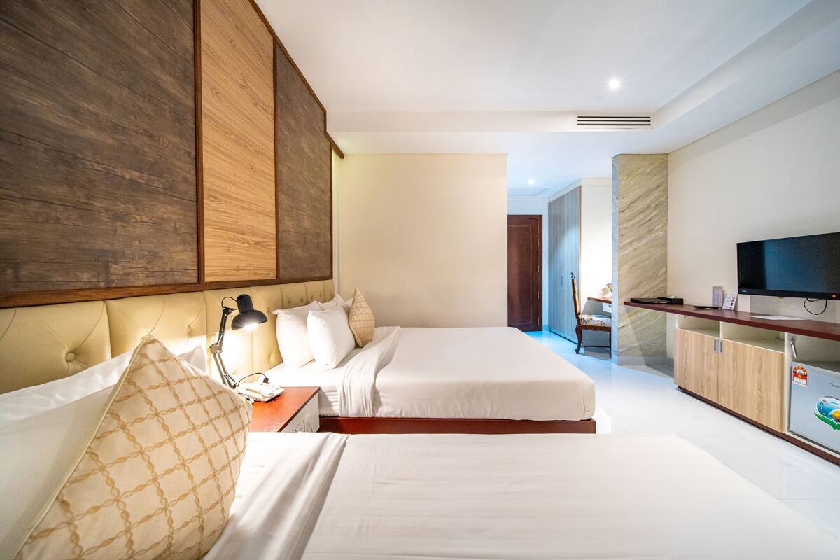 Quarto de hotel moderno com uma cama grande, uma mesa com luminária, televisão e minibar.
