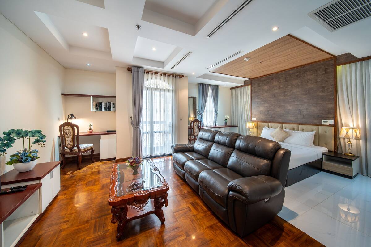 Quarto de hotel moderno com sofá de couro, mesa de centro de madeira, cama com roupa de cama branca e um espelho grande.