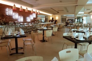 Restaurante com várias mesas e cadeiras, algumas com toalhas e guardanapos brancos.