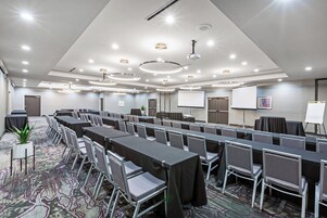 Uma sala de conferência com várias mesas e cadeiras, uma tela de projetor e um quadro branco.