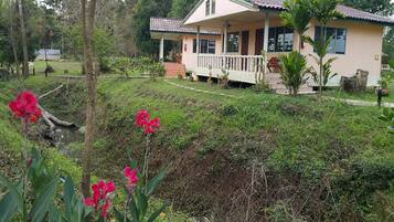 Uma casa térrea com varanda, rodeada por vegetação exuberante e um pequeno lago.