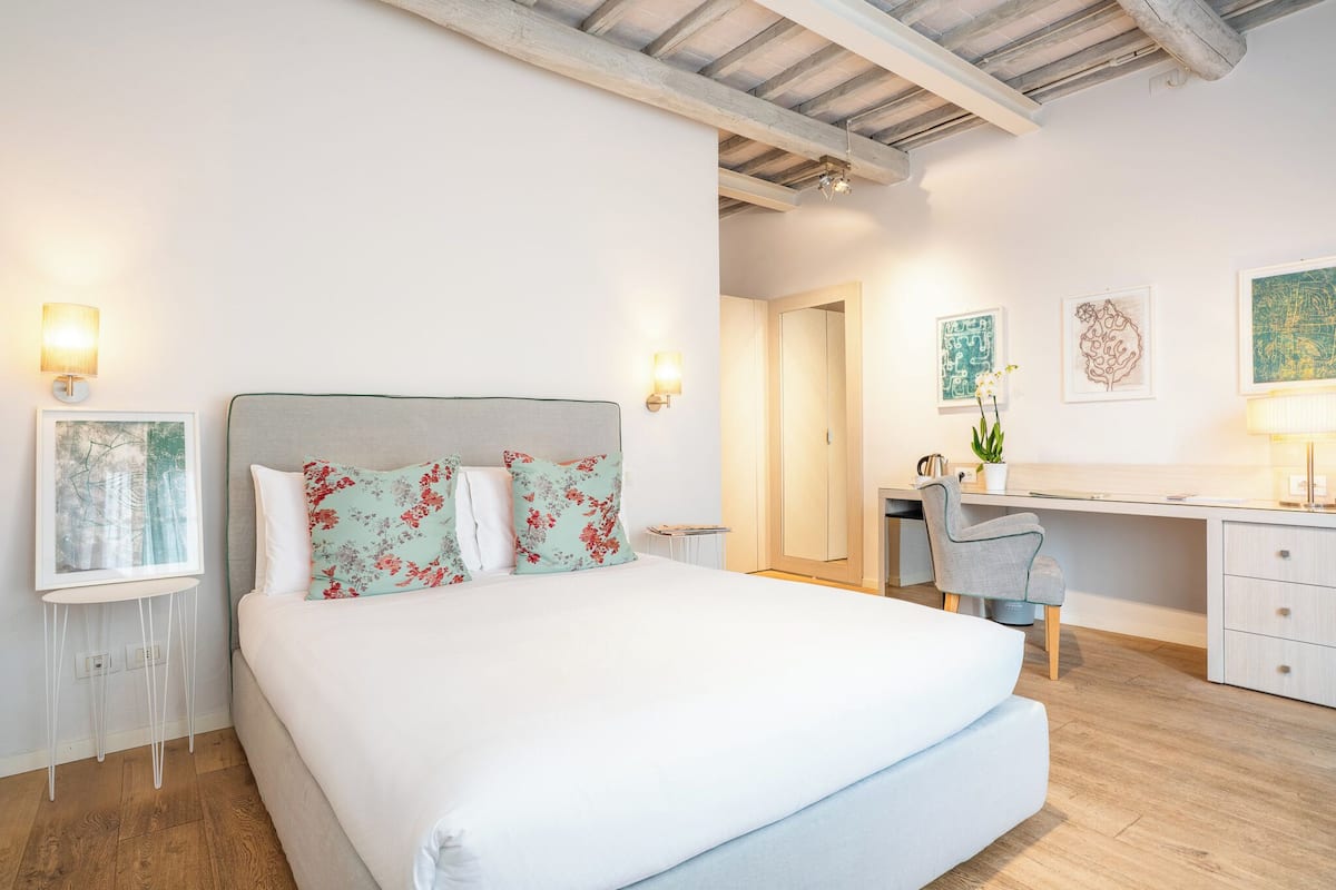 Um quarto com cama, mesas de cabeceira, escrivaninha e uma cadeira.