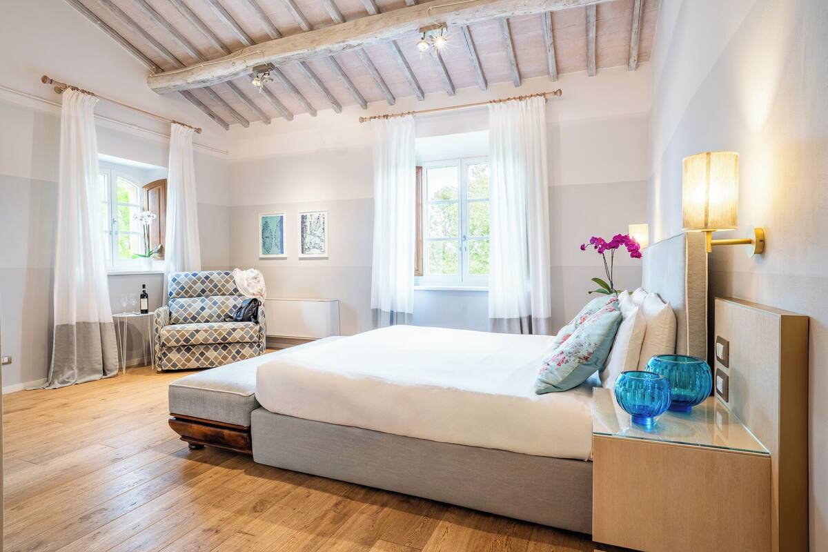 Quarto com cama, cadeira, mesa de cabeceira e janela.