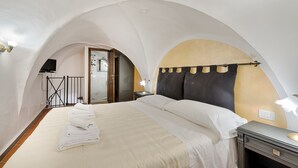 Um quarto com uma cama grande, uma mesinha de cabeceira e uma TV fixada na parede.