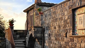 Um edifício de pedra com uma escadaria que leva a uma varanda, uma chaminé e uma janela decorativa.