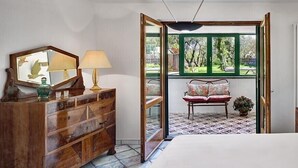 Quarto com cômoda de madeira, uma cama, janela com vista para o verde e piso estampado.
