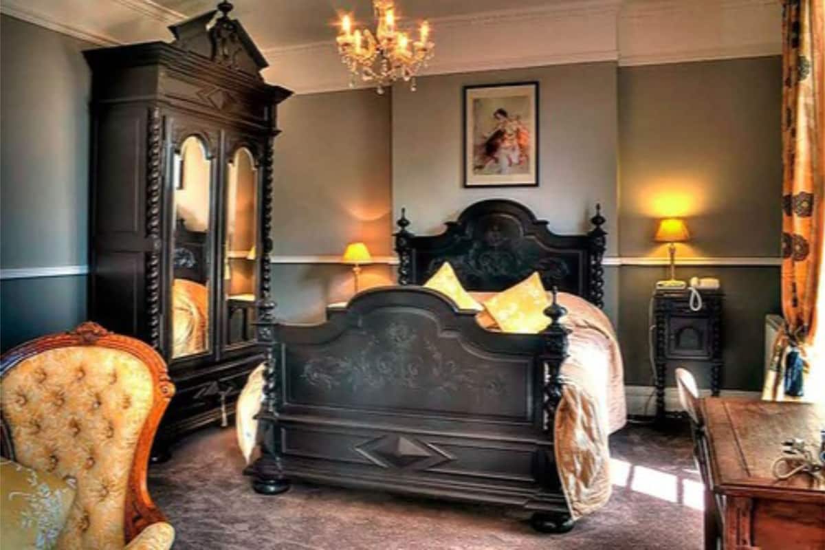 Um quarto clássico com uma cama grande, mobiliário de madeira ricamente decorado e um candelabro.