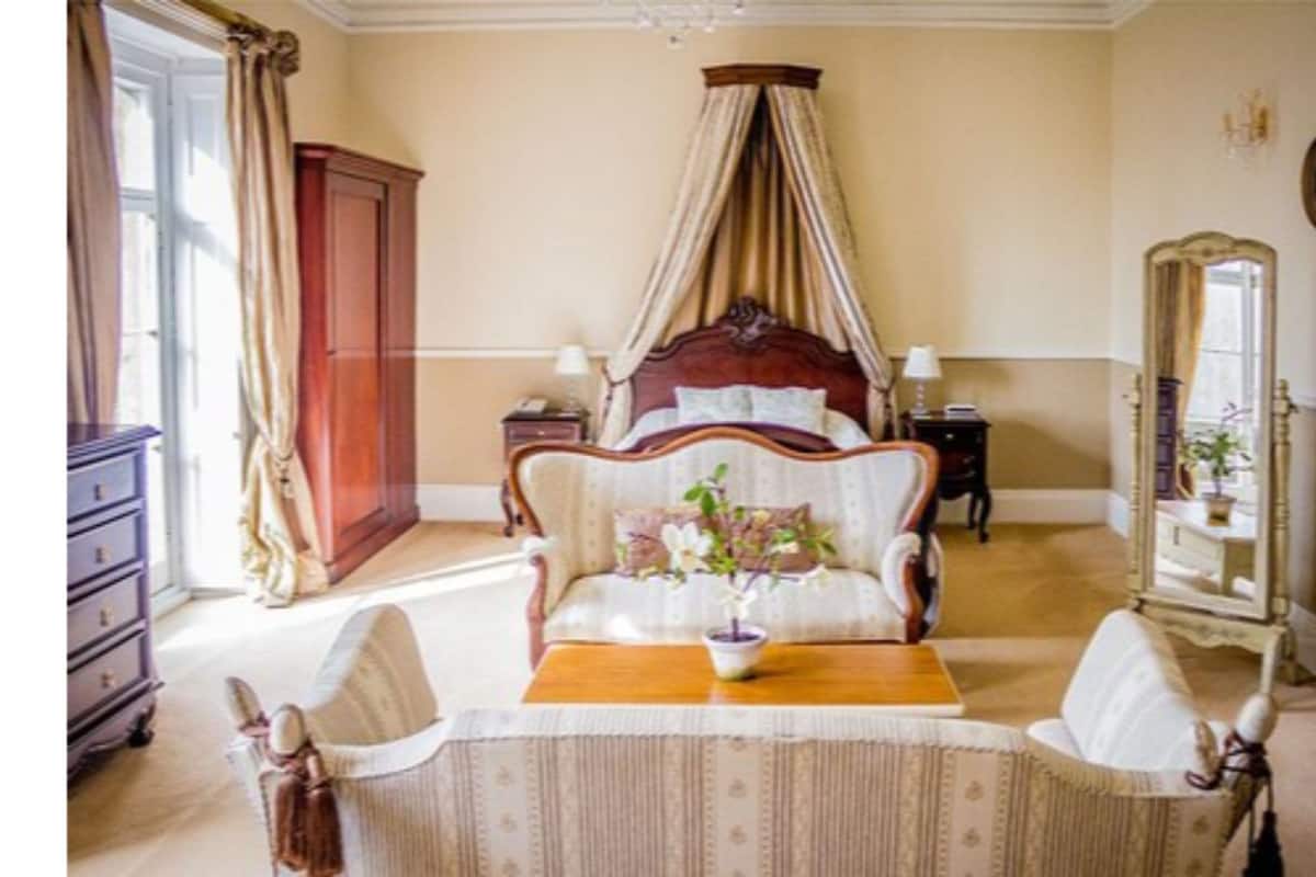 Quarto com uma cama de dossel, uma mesa de cabeceira de madeira, cômoda e espelho.