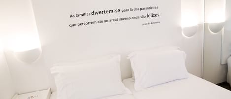 Quarto de hotel com cama, almofadas brancas, manta verde e parede com uma frase em português.