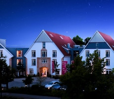 Uma fileira de casas modernas com estilos arquitetônicos distintos, incluindo um edifício de destaque com telhado vermelho e entrada visível.