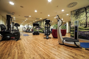 Uma academia com equipamentos de ginástica, piso de madeira e um mural com tema de floresta.