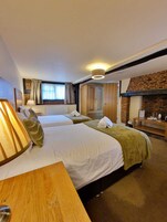 Quarto de hotel com duas camas, uma escrivaninha de madeira, uma parede de tijolos e uma lareira.