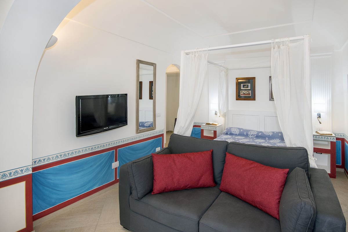 Quarto com cama, televisão, sofá e mesa de cabeceira.