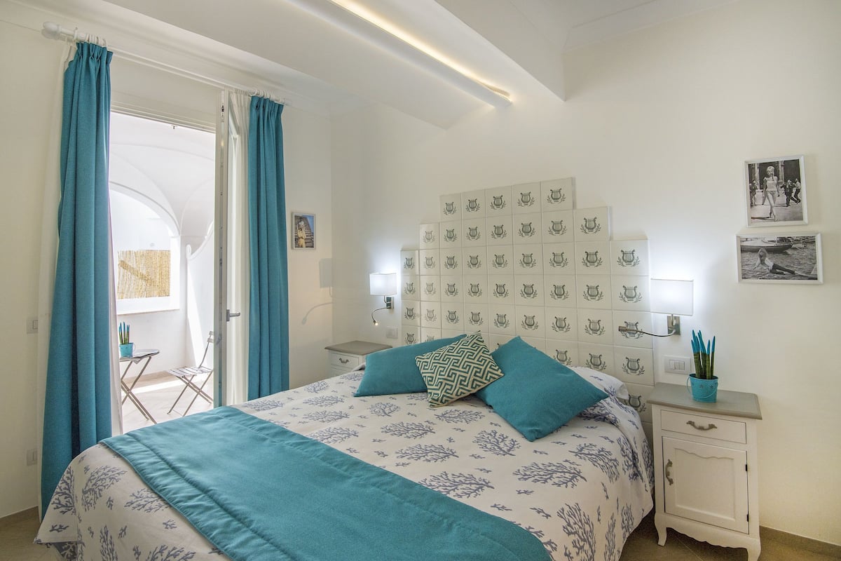 Quarto com cama, cortinas, mesa de cabeceira e quadros na parede.