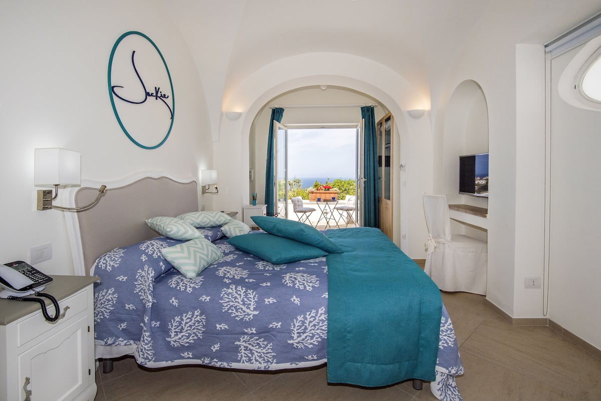 Quarto com cama, telefone ao lado da cama, televisão na parede e varanda com vista.