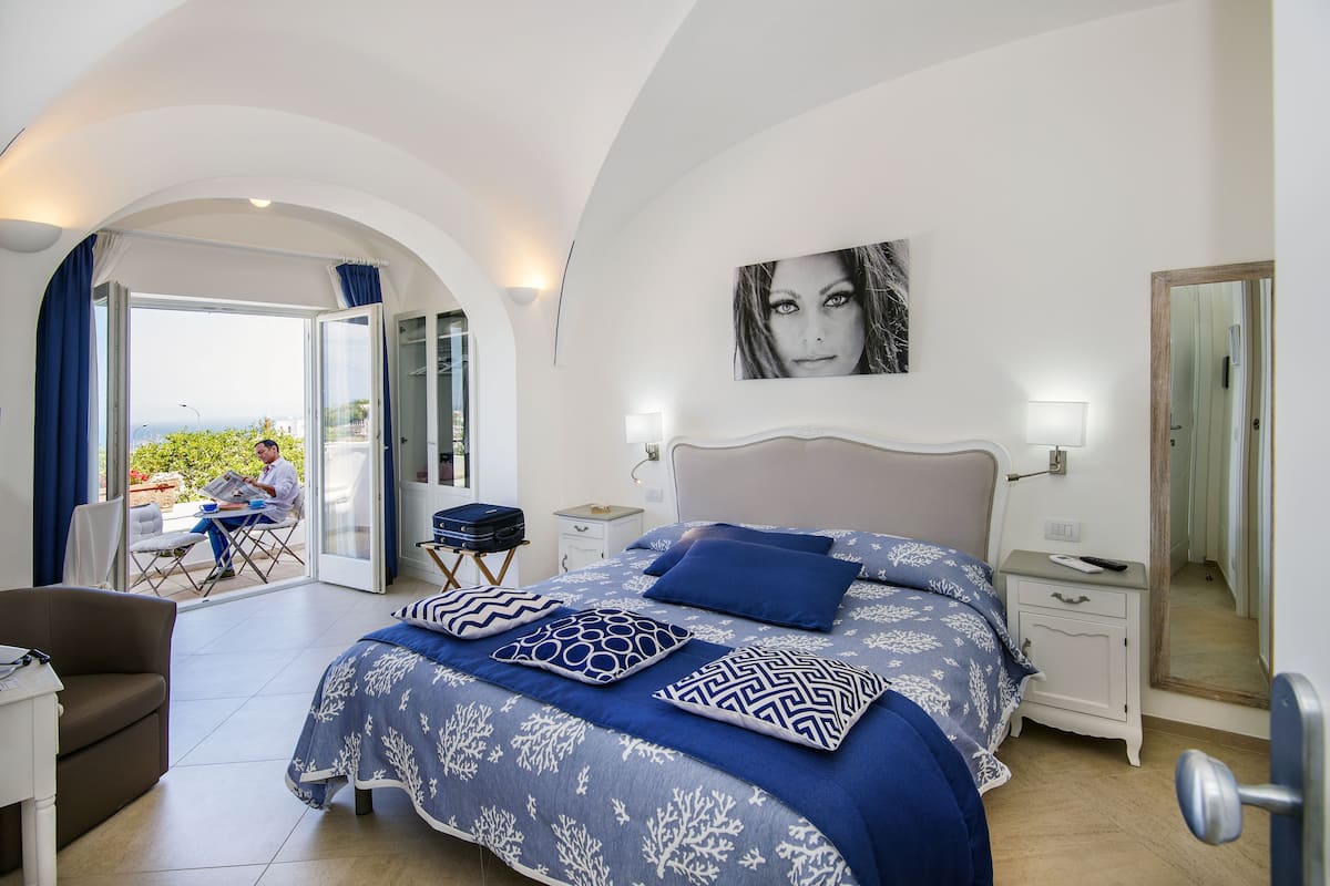 Quarto com uma cama grande, escrivaninha e varanda com vista.