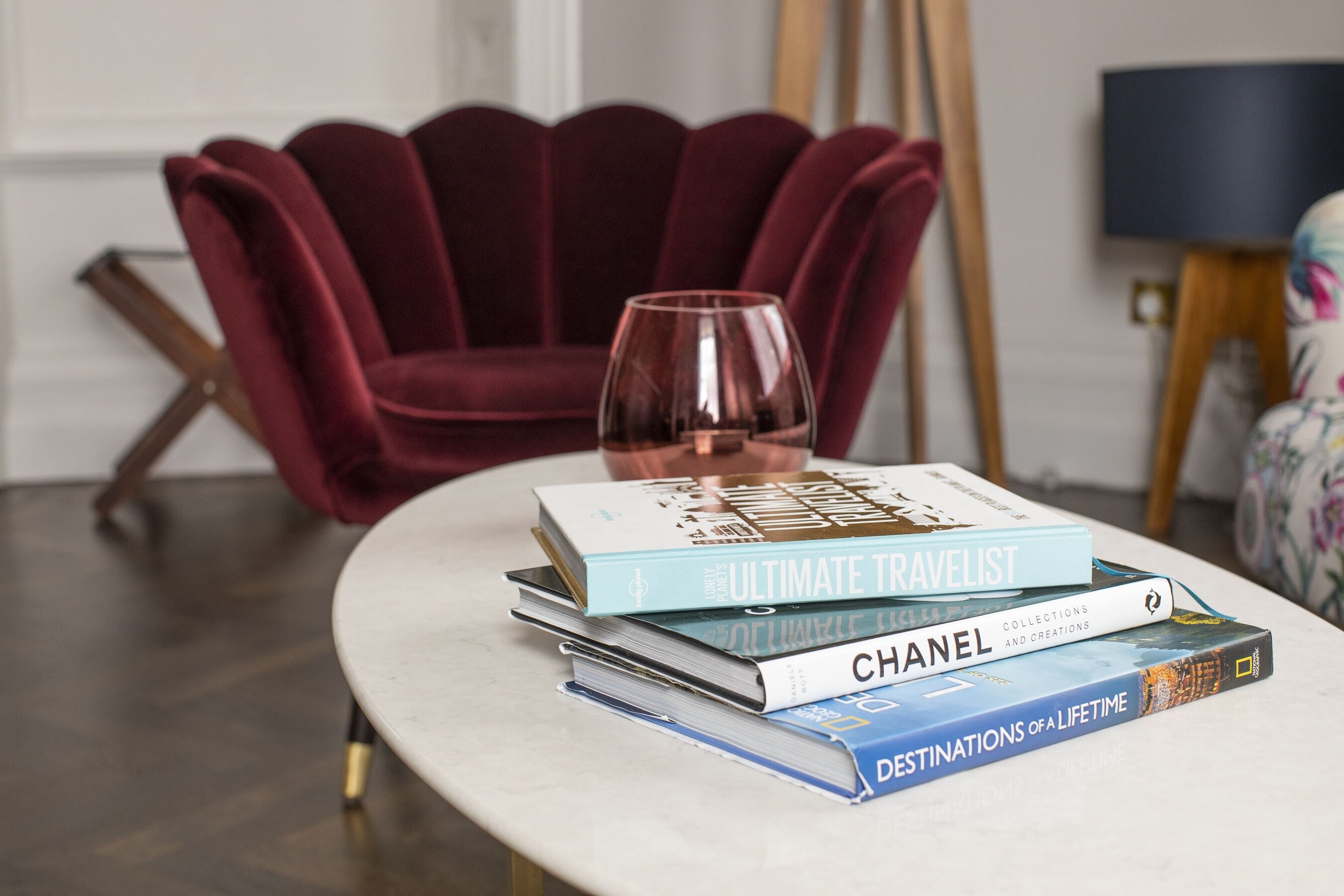Uma pilha de livros sobre uma mesa redonda com uma taça de vinho em cima.