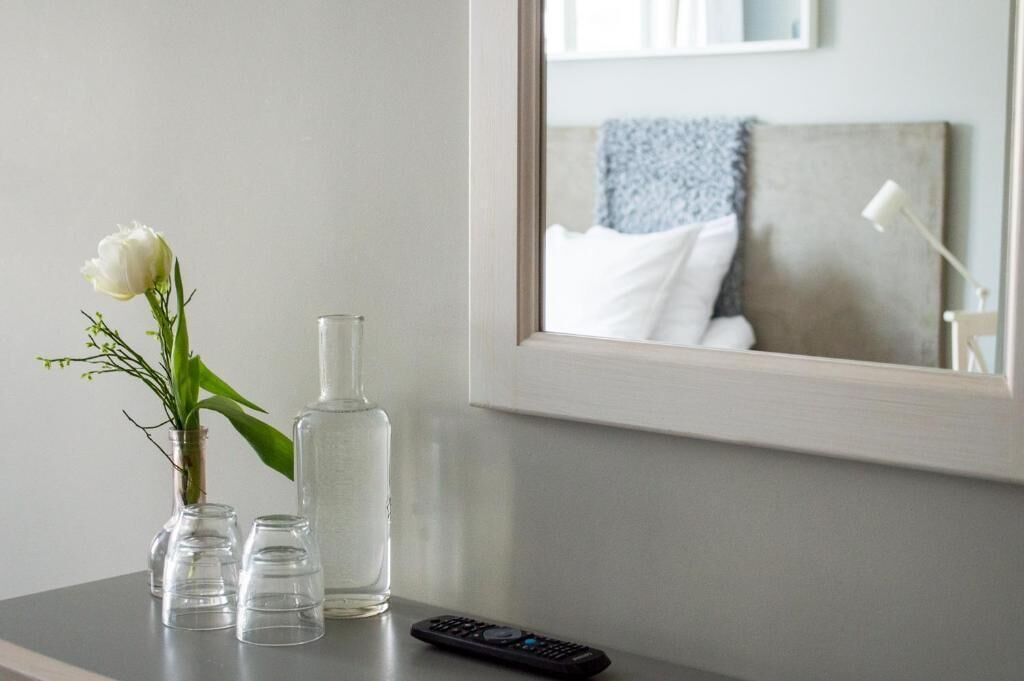 Uma mesa de cabeceira com um vaso de flores brancas, uma garrafa transparente e um controle remoto.
