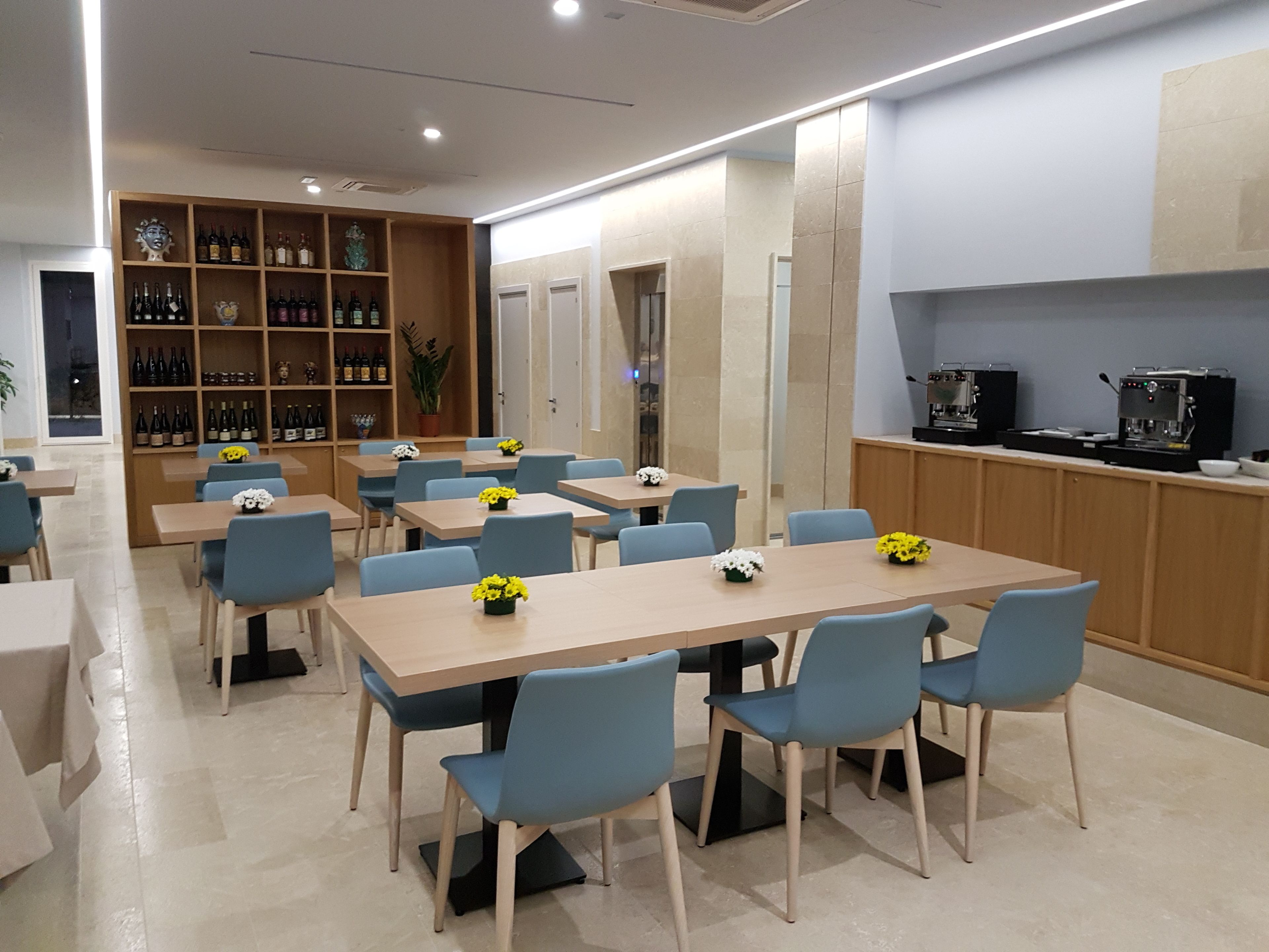 Um restaurante com várias mesas e cadeiras, uma área de exposição de vinhos e uma máquina de café.