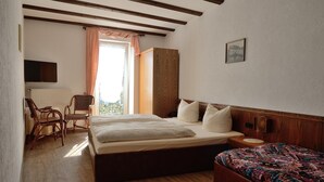 Quarto com uma cama grande, uma cama menor, uma escrivaninha com cadeira e uma janela com cortinas.