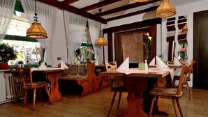 Uma zona de refeições acolhedora com mobiliário de madeira, candeeiros pendentes e plantas em vasos.