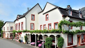Um edifício de estilo europeu tradicional com um terraço de café, mesas ao ar livre e uma placa indicando que é um restaurante.