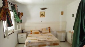Quarto com cama, duas mesas de cabeceira, luminária pendente e janela com cortinas.