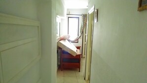 Um corredor estreito com uma cama no final, um radiador e uma porta com cortina.