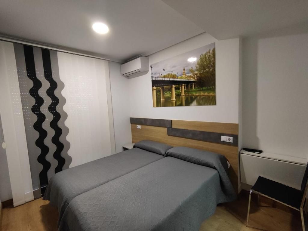 Quarto com cama, ar-condicionado fixado na parede, pintura de uma ponte e cabeceira de madeira.