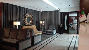 Um hall de hotel moderno com um sofá, poltronas, uma mesa redonda e um espelho grande.
