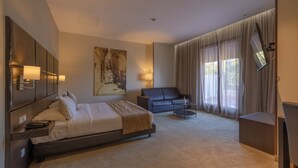 Quarto de hotel moderno com cama grande, sofá, mesa pequena e televisão.