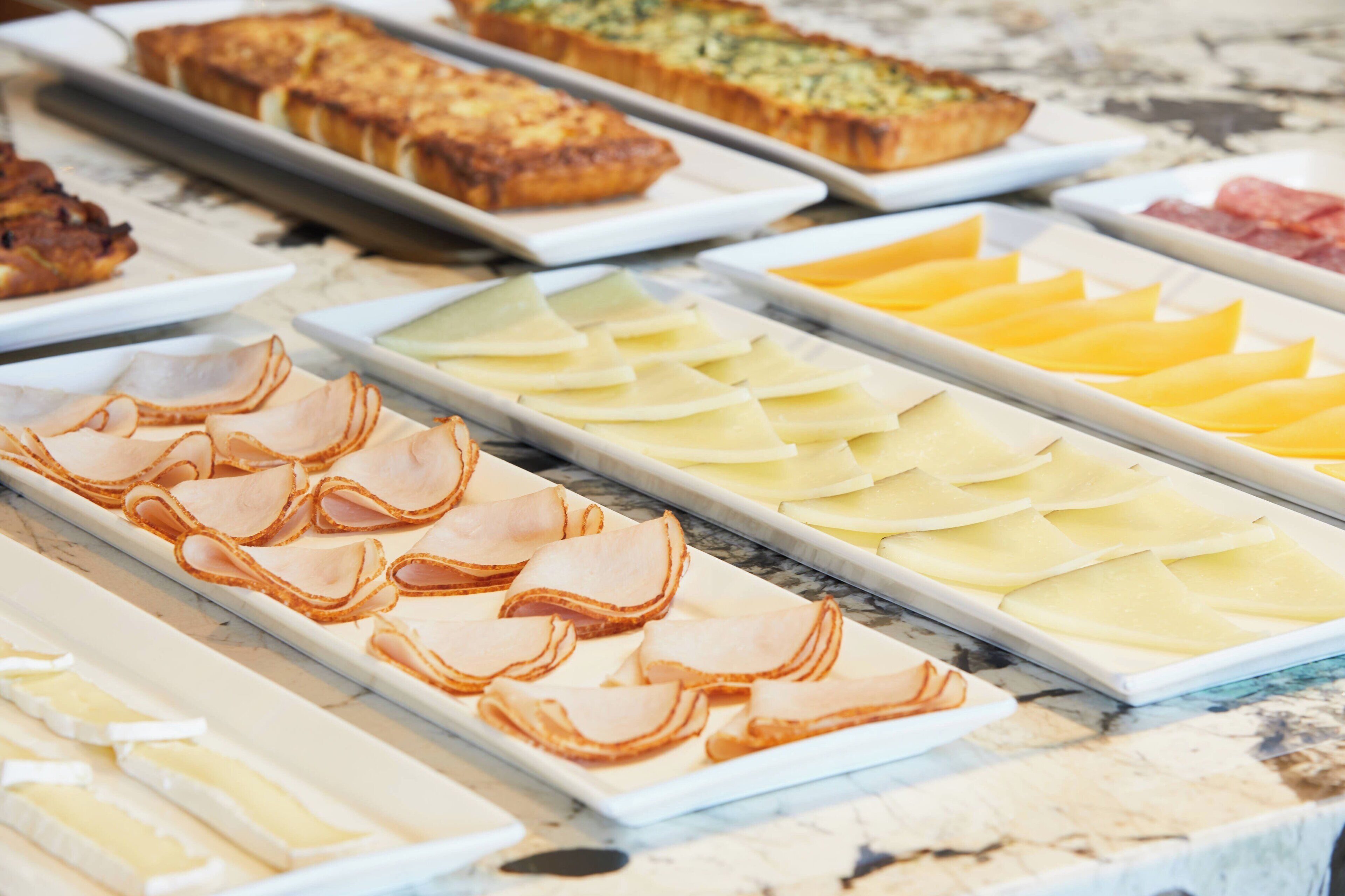 Buffet com diversos itens, incluindo carnes fatiadas, queijos e doces.