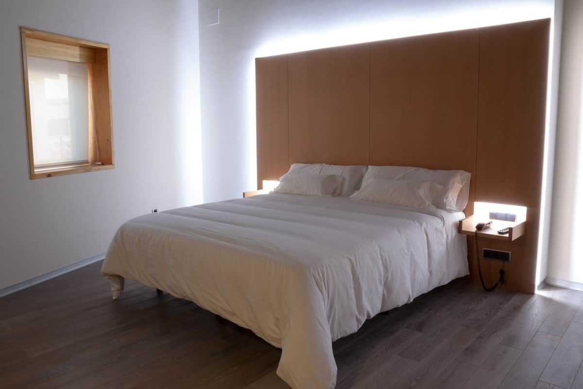 Quarto com uma cama grande, cabeceira de madeira, mesas de cabeceira e uma janela.