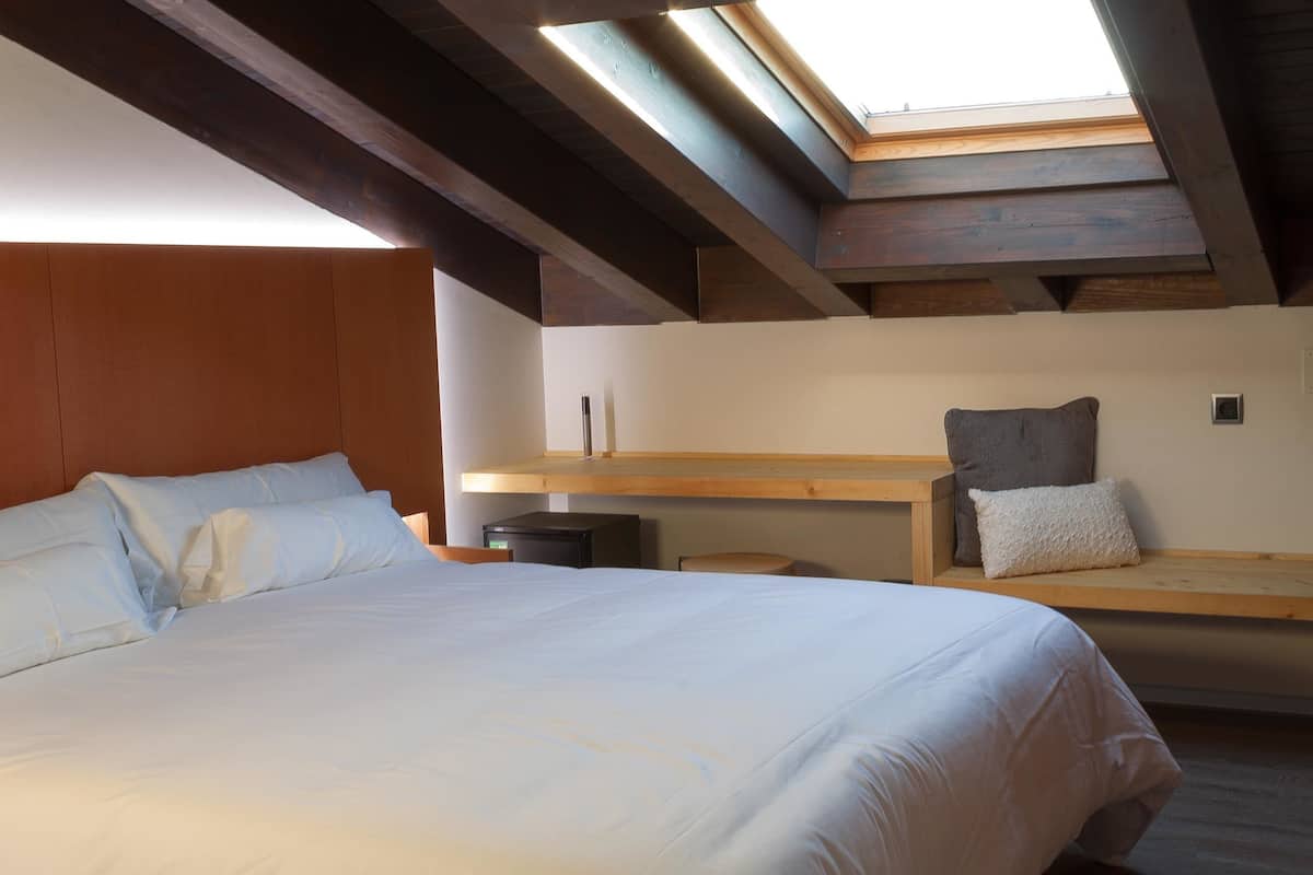Quarto com uma cama grande, um banco de madeira e um claraboia.