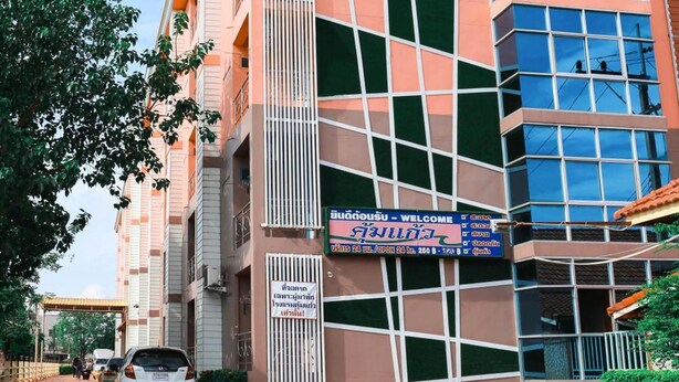 Um edifício de vários andares com fachada moderna, combinando painéis de vidro e partes sólidas. Há uma placa com texto em tailandês indicando o nome do edifício e possivelmente sua função.