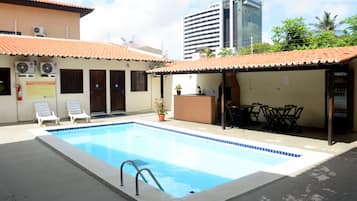Piscina com espreguiçadeiras, área de estar coberta e um edifício com telhado telhado.