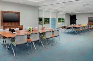 Uma sala de conferências com uma mesa comprida, cadeiras, uma televisão e uma janela grande.