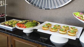 Buffet com diversos pratos, incluindo legumes grelhados, carnes e aperitivos.