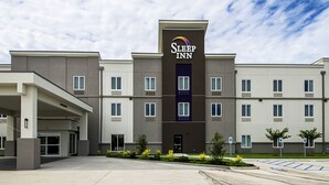 Um hotel Sleep Inn com design moderno, apresentando uma entrada central com detalhe vertical escuro, várias janelas e um estacionamento com vagas demarcadas.