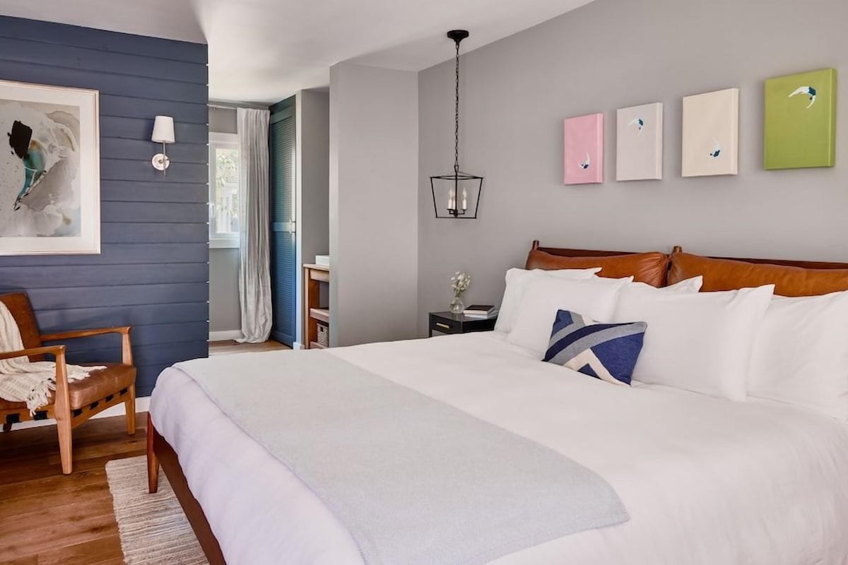 Quarto com uma cama grande, uma cadeira, uma mesa de cabeceira e um lustre.
