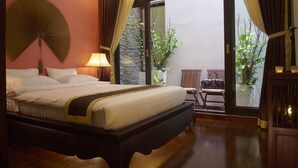 Quarto com uma cama grande, luminária de cabeceira, ventilador e vista para uma varanda com plantas.