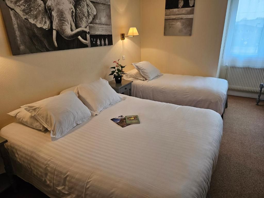 Quarto de hotel com duas camas, uma mesa de cabeceira com abajur e um quadro grande de um elefante na parede.
