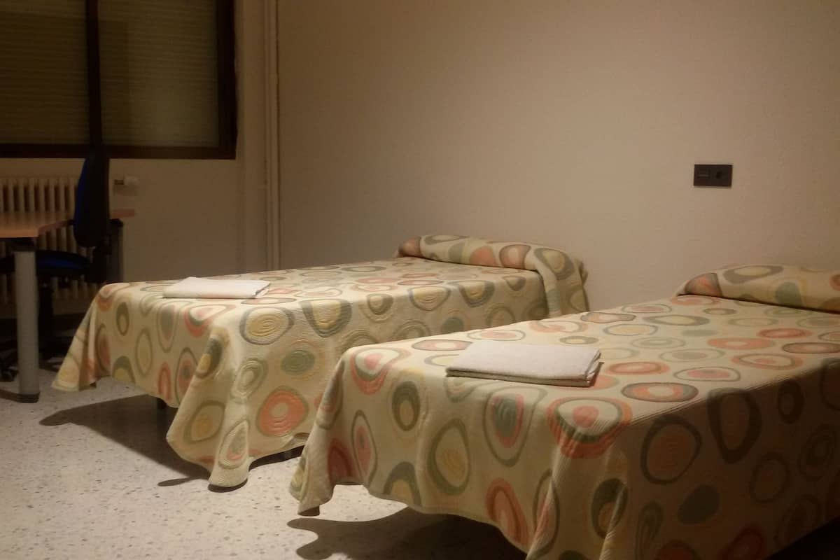 Quarto pequeno com duas camas, uma cadeira e um radiador.