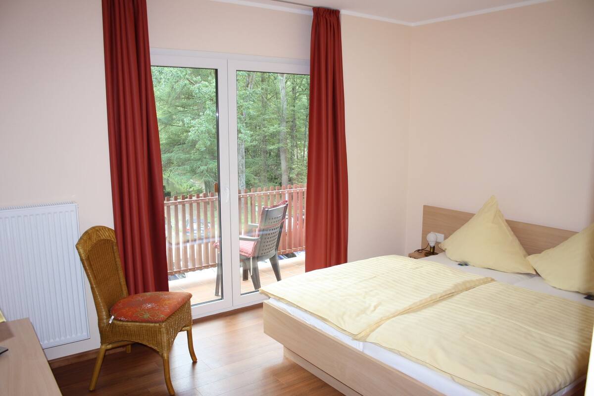 Um quarto com uma cama, uma cadeira, uma janela com cortinas e vista para uma varanda.
