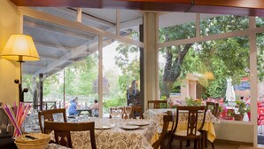 Um restaurante com mesas ao ar livre, grandes janelas e vista para o jardim.