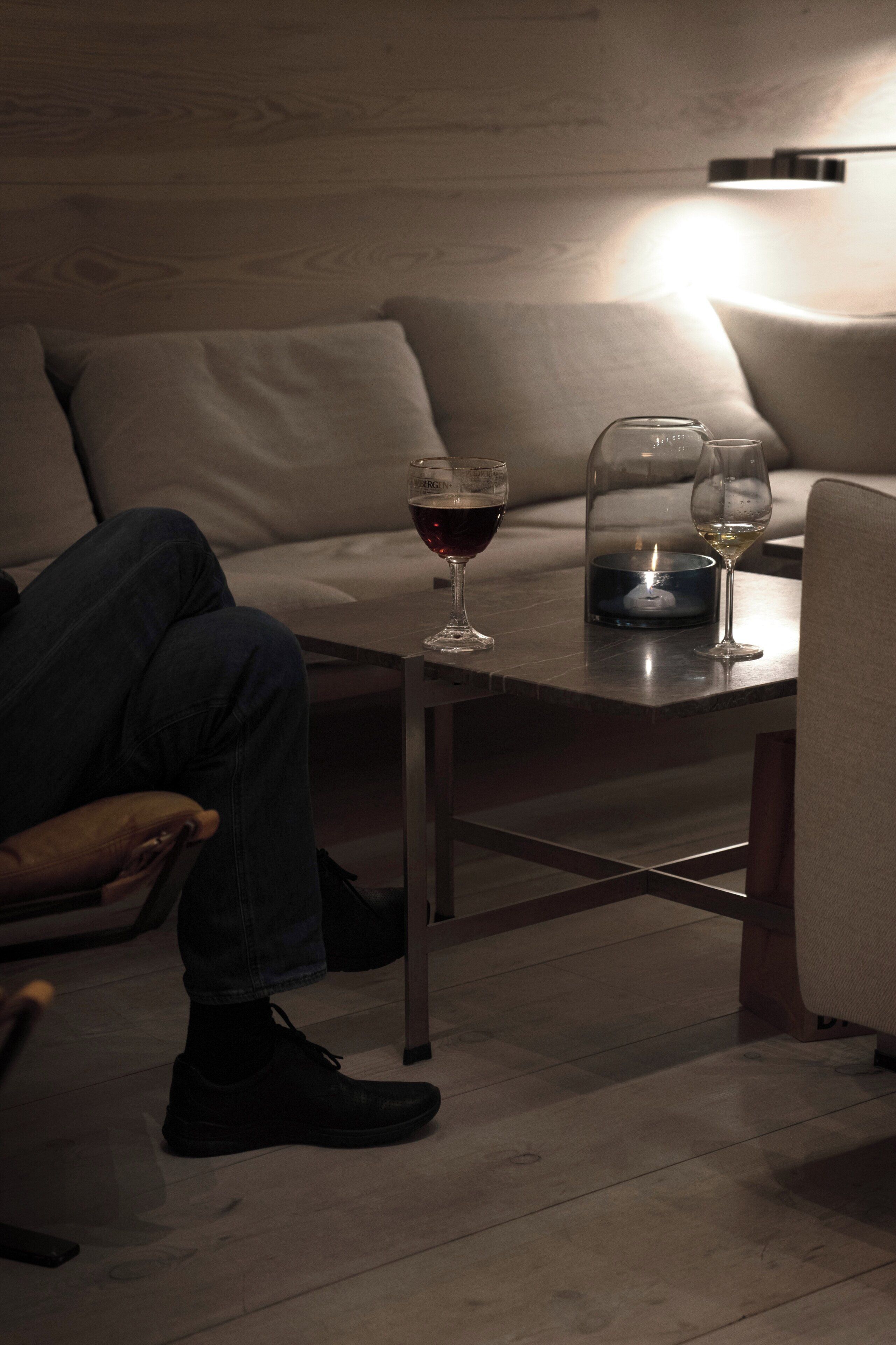 Um quarto com pouca luz, um sofá, uma mesa com duas taças de vinho e uma vela.