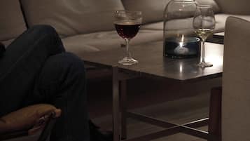 Um quarto com pouca luz, um sofá, uma mesa com duas taças de vinho e uma vela.